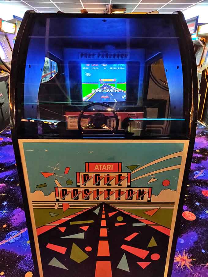 The legendary Pole Position cabinet stands ready for action, its steering wheel worn smooth by decades of virtual racers chasing that perfect lap time.