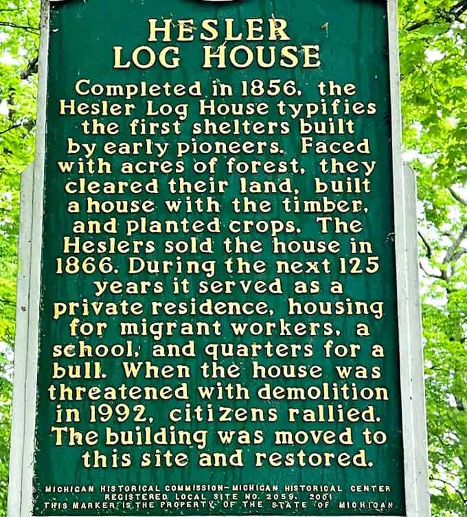 This green sign tells the Hesler Log House story - from pioneer home to school to bull quarters, before citizens rescued it from demolition.