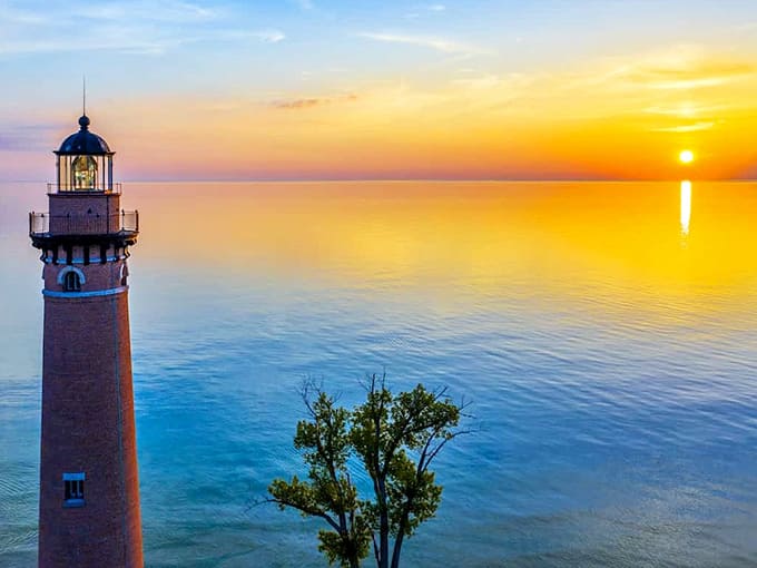 Little Sable Point Lighthouse stands sentinel against a technicolor sunset, its brick tower guiding mariners along Lake Michigan's shore since 1874.