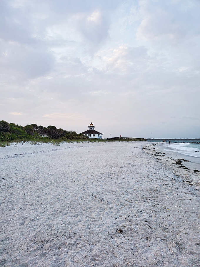 The lighthouse appears almost shy in the distance, a white speck against the vast beach, inviting visitors to come closer and discover its secrets.