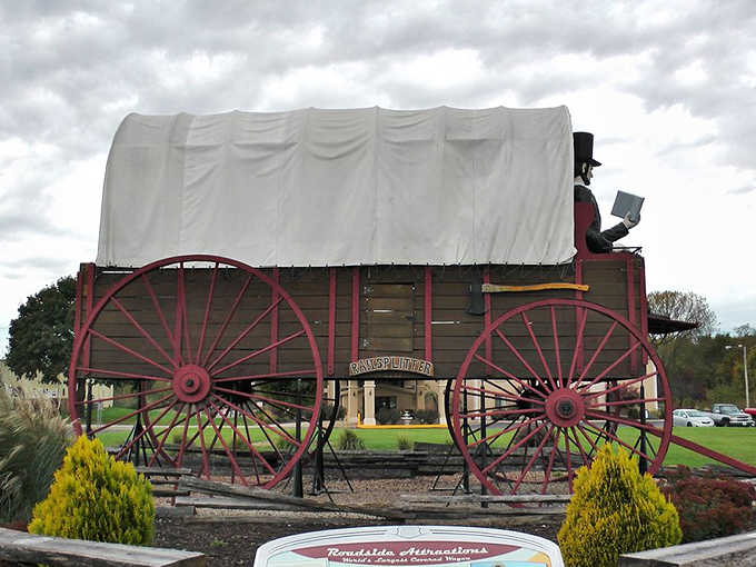 The wagon's massive wooden construction and canvas top showcase pioneer ingenuity, just supersized for modern roadside attraction enthusiasts.