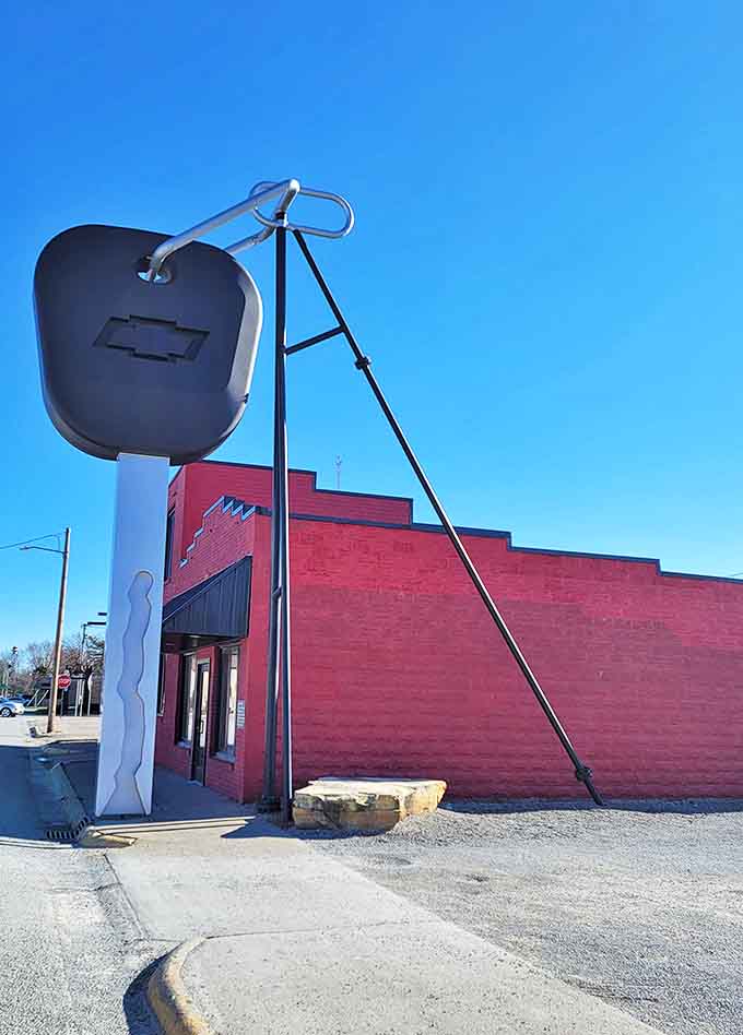 Bathed in sunshine, the giant key creates dramatic shadows across the sidewalk, turning an ordinary day into a surreal roadside adventure.