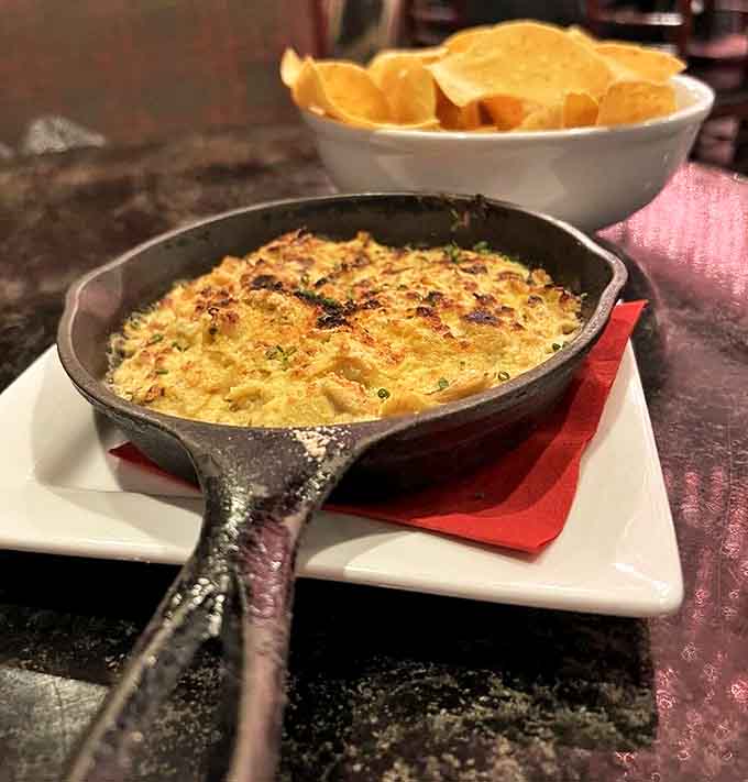 Bubbling artichoke dip arrives in a cast-iron skillet, creating a tableside moment of anticipation before the inevitable chip-dipping frenzy begins.