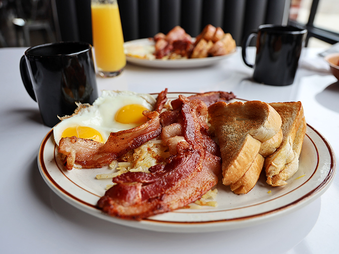 Two sunny-side-up eggs flanked by crispy bacon strips and golden toast – the breakfast trinity that's been curing hangovers since time immemorial.
