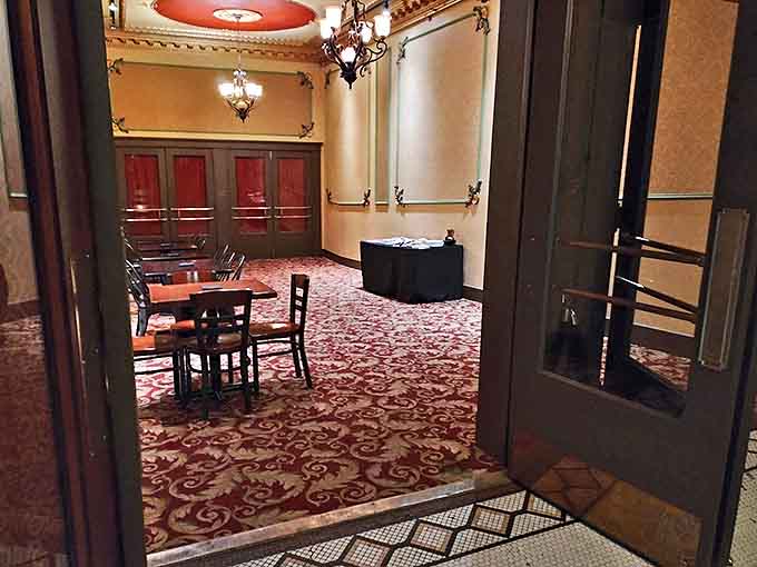 Elegant chandeliers illuminate the dining area's rich red carpet, where vintage charm meets modern comfort in a space perfect for pre-show gatherings.