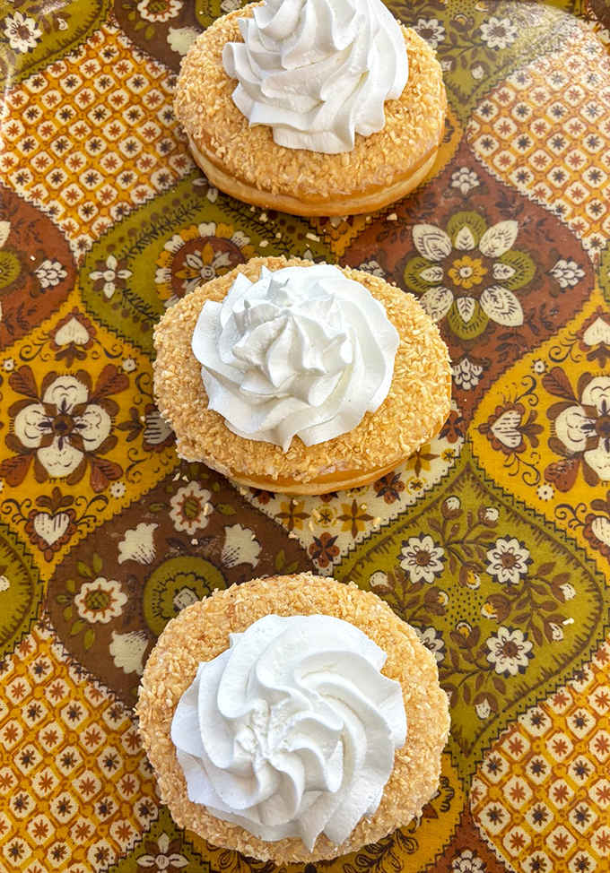 Italian Cream Cake Donuts crowned with coconut and whipped cream &ndash; proof that sometimes the best international diplomacy happens through pastry.