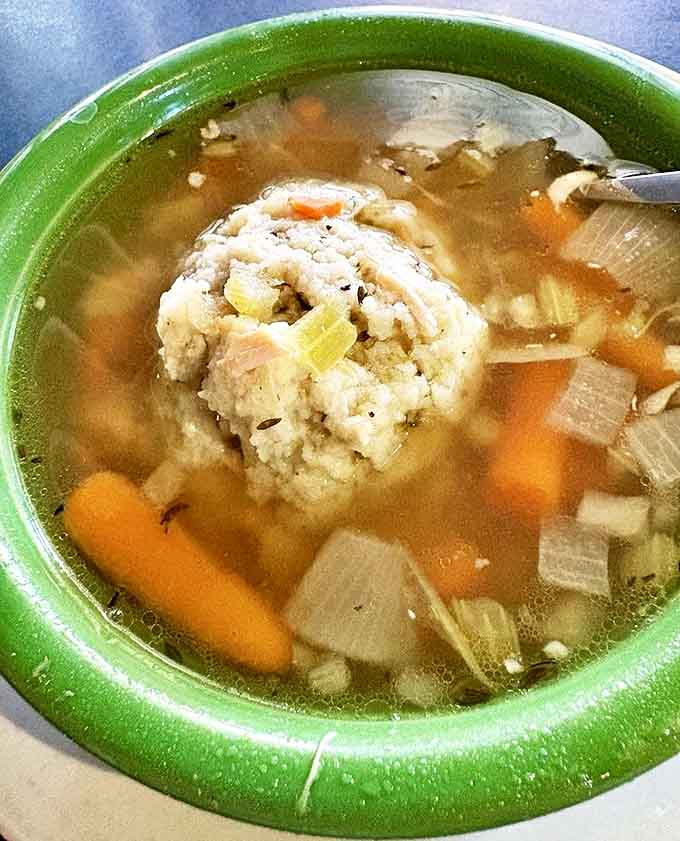 A perfect matzo ball floats like a dumpling planet in a galaxy of golden broth, surrounded by tender vegetables and chicken.