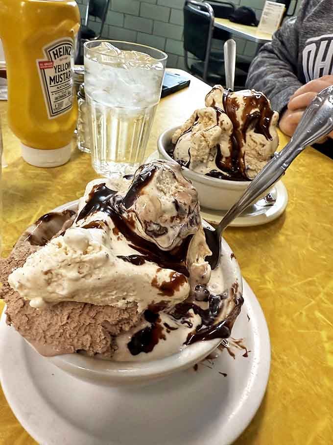 Hot fudge cascades over cold cream like chocolate lava, creating that perfect temperature tango that makes your taste buds do the cha-cha.