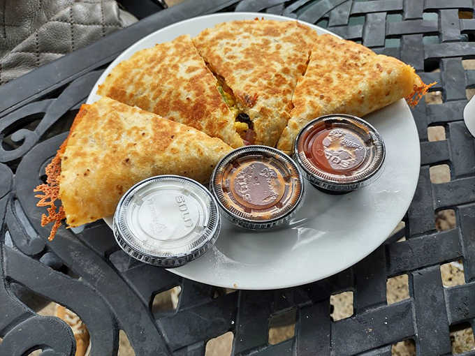 Golden-brown quesadillas arrive with a trio of dipping sauces, creating a breakfast triangle of deliciousness that demands to be photographed before devoured.