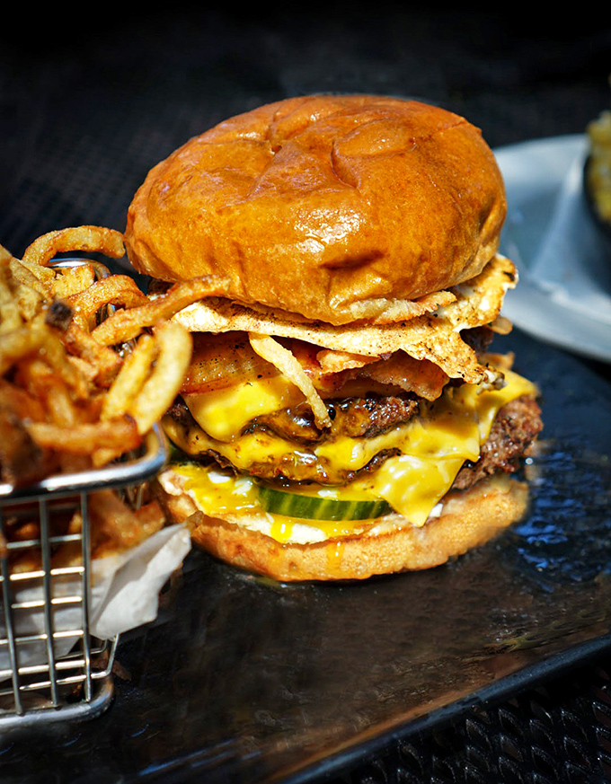 Towering achievement in burger architecture &ndash; melty cheese cascades over perfectly seared patties on a golden brioche throne.