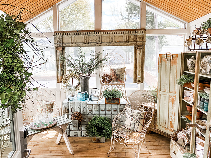 Sunlight streams through glass walls in this dreamy garden room, where vintage furniture and architectural salvage create a Pinterest-worthy retreat.