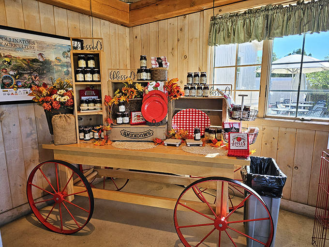 Rustic wooden cart displays showcase seasonal jams like jewels on a treasure wagon, the red wheels adding a touch of farmhouse charm.