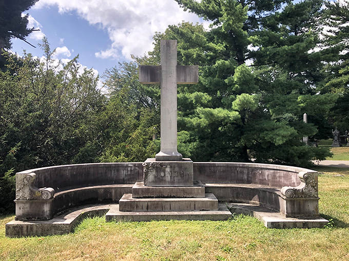 A contemplative stone cross sits surrounded by a curved bench, inviting visitors to pause and reflect on life's journey.