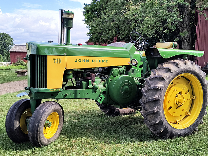 The John Deere 730 tractor gleams in its iconic green and yellow, a mechanical time capsule from farming's mechanized revolution.