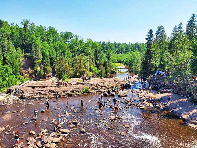Visitors explore the rocky riverbed during summer, when lower water levels transform the falls area into nature's perfect playground for rock-hoppers of all ages.
