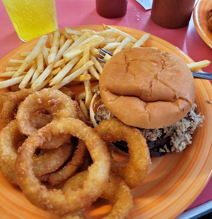 A perfect trifecta of comfort: juicy BBQ sandwich, golden fries, and crispy onion rings that make you question why you'd ever eat anything else.