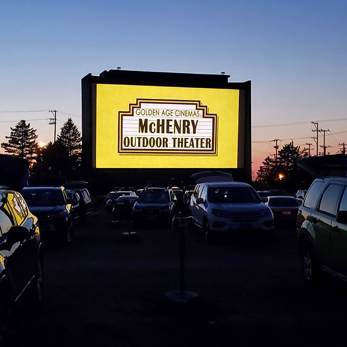 The McHenry Outdoor Theater's glowing marquee proudly announces "GOLDEN AGE CINEMAS," a beacon of nostalgia against the twilight sky.