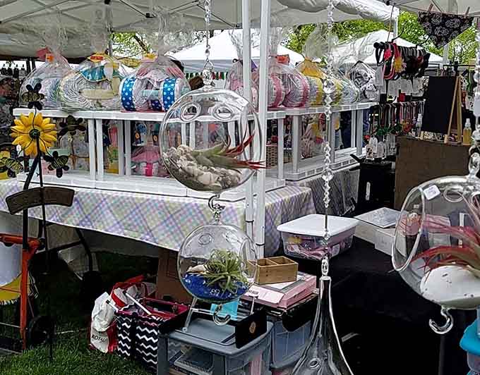 Shoppers wander between market booths under dappled sun.
