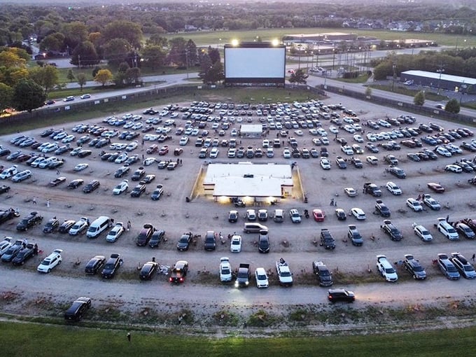 An aerial view reveals hundreds of cars arranged in perfect rows, creating a temporary city of movie lovers united by the glowing screen at the center.