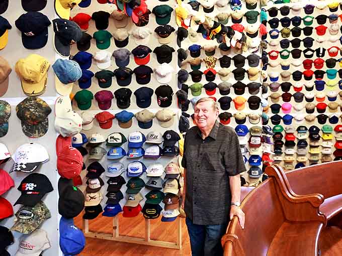 A visitor smiles amid the collection, perhaps spotting a familiar logo or remembering a hat just like one they wore decades ago.