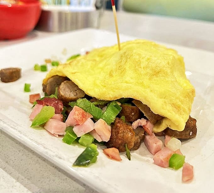 This isn't just any omelet – it's a perfectly folded yellow canvas filled with savory treasures and garnished with fresh diced vegetables.