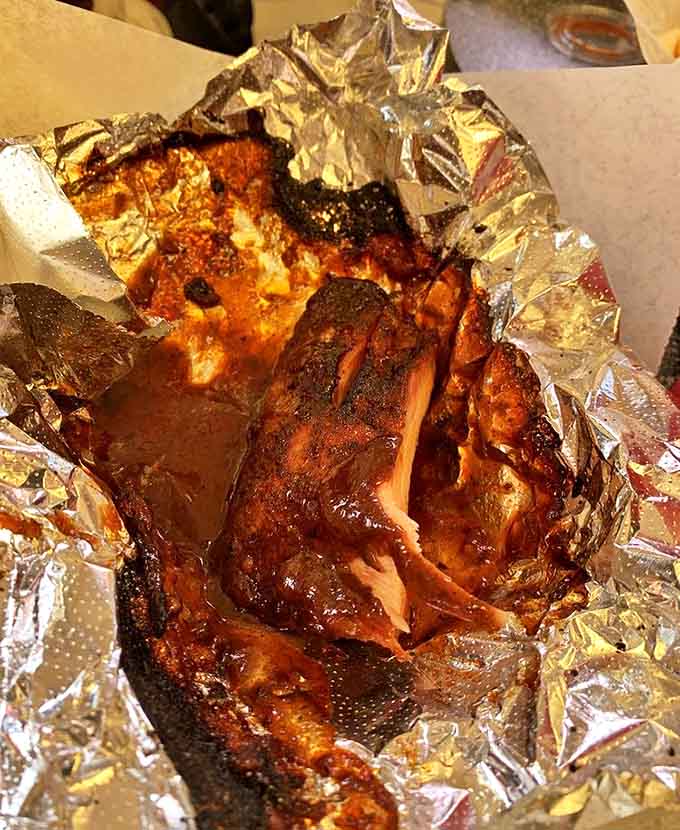 Wrapped in foil that barely contains their glory, these ribs showcase that perfect pink smoke ring that makes barbecue enthusiasts weak at the knees.