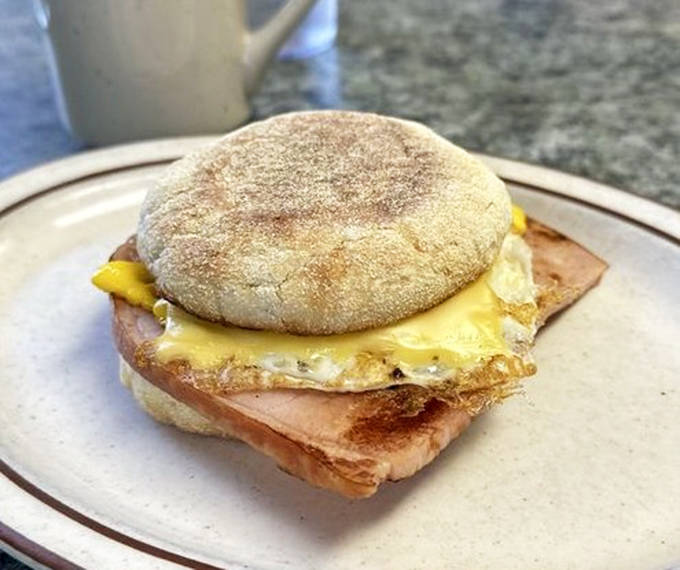 A breakfast sandwich that understands the architecture of morning perfection: runny egg, melted cheese, and caramelized ham edges on a sturdy English muffin.