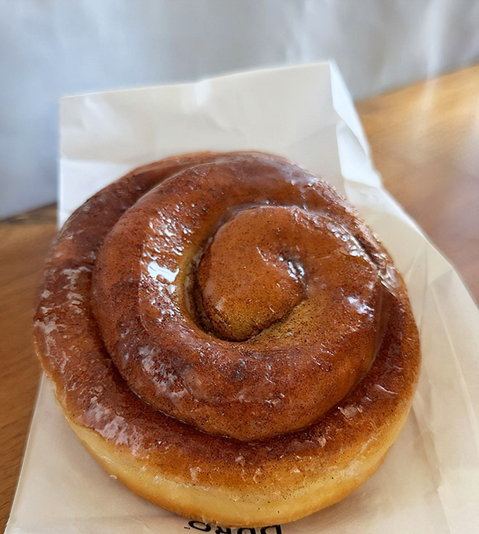 The cinnamon roll spirals hypnotically, its layers promising to pull apart with that satisfying stretch that makes sharing both possible and deeply regrettable.