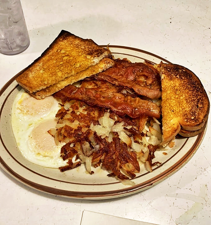 The breakfast trinity: perfectly cooked eggs, crispy bacon, and golden hash browns that could make a potato farmer weep with pride.