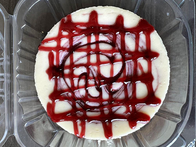 This raspberry lemon cheesecake wears its ruby-red topping like jewelry, the vibrant sauce creating a perfect sweet-tart balance against the creamy canvas below.