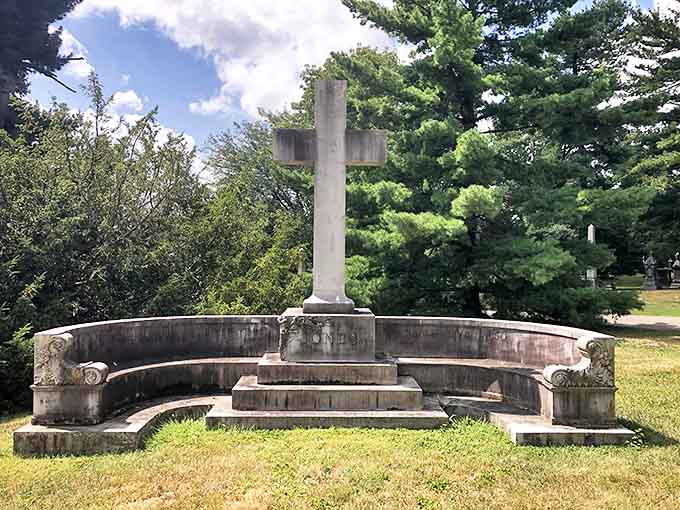 A stone cross monument creates a perfect symmetry with its circular bench, inviting quiet contemplation in the cemetery's peaceful grounds.