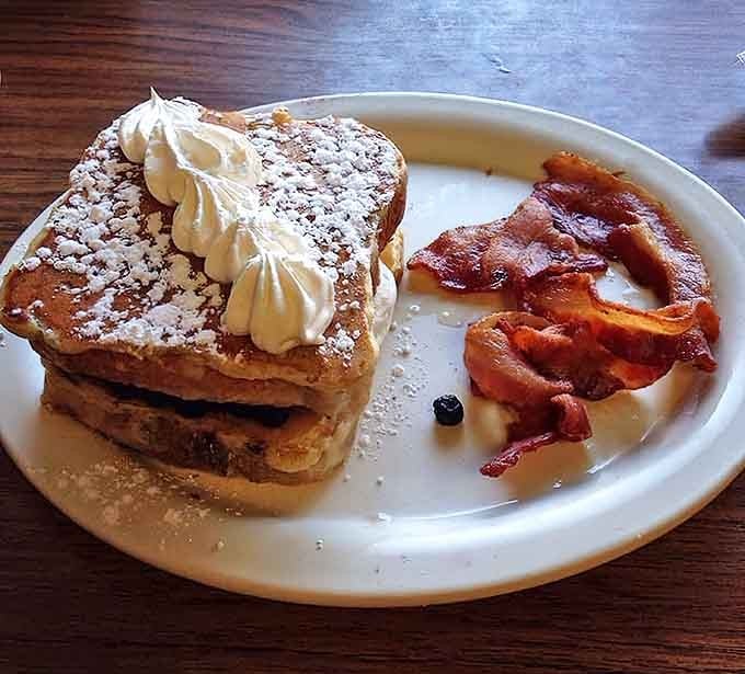The perfect breakfast trinity: stuffed French toast dusted with powdered sugar, a dollop of whipped cream, and crispy bacon on the side.