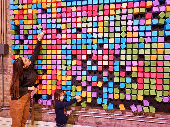 Visitors interact with a colorful wall of movable blocks, turning a simple concept into an ever-changing canvas of collaborative creativity.