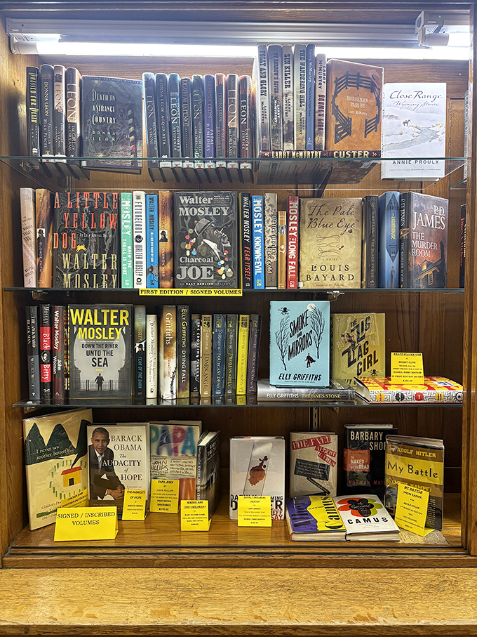 First editions and signed books rest behind glass, their yellow tags signaling literary treasures that collectors might search years to find elsewhere.