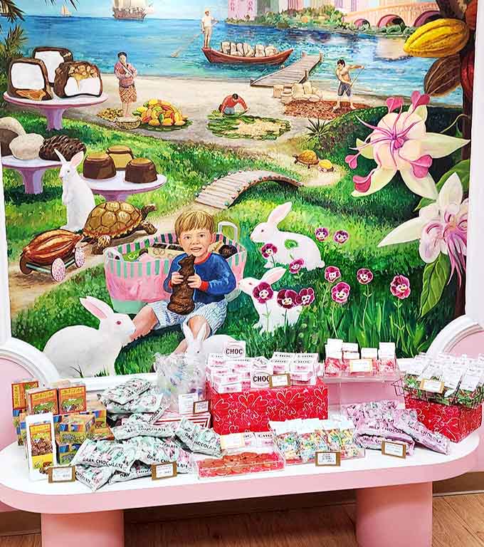 A whimsical mural transports visitors to a fantastical chocolate world where bunnies frolic and cocoa grows alongside magical cityscapes.