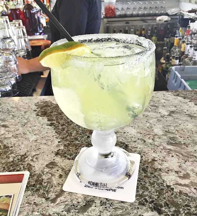 A salt-rimmed margarita schooner catches the light, its lime-green contents offering a tangy counterpoint to savory pizza flavors.