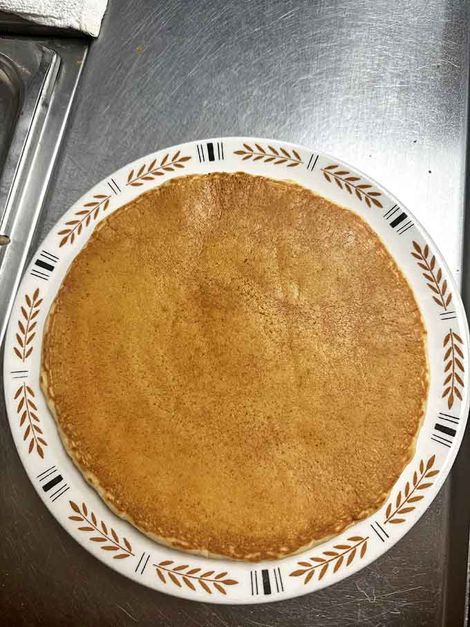 This golden pancake stretches to the plate's edge, a perfect circle of breakfast joy that's just begging for a maple syrup waterfall.