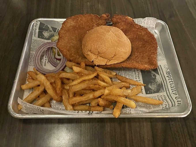 The breaded pork tenderloin extends beyond its bun borders in proper Midwestern fashion – a crispy testament to heartland hospitality.
