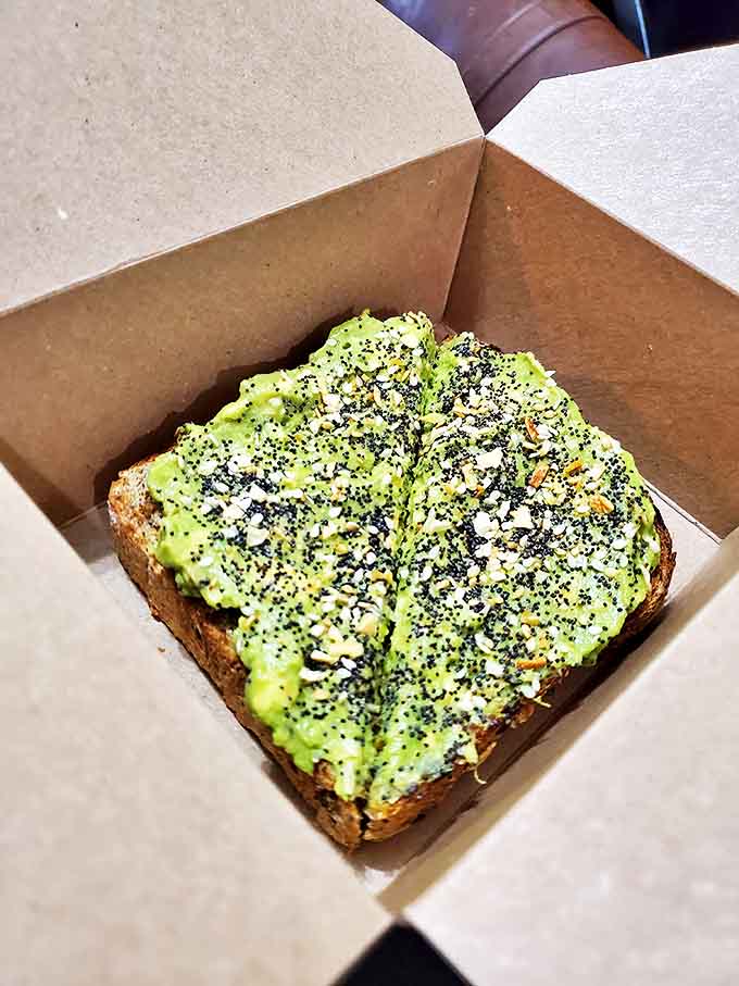 Avocado toast elevated to an art form, with vibrant green spread adorned with black sesame seeds and spices on hearty artisanal bread.