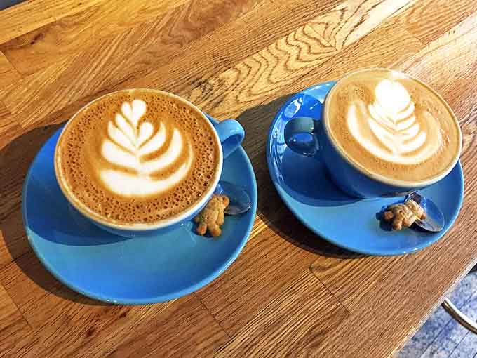 Bright blue cups cradle perfectly crafted cappuccinos, each topped with intricate latte art and served with a tiny cookie surprise.