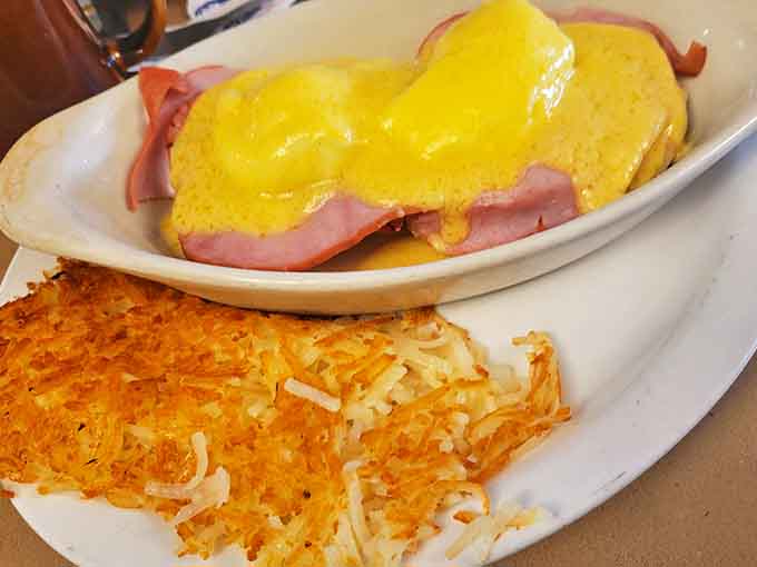 Eggs Benedict done right: velvety hollandaise cascading over ham and perfectly poached eggs, with hash browns crisped to golden-brown perfection.