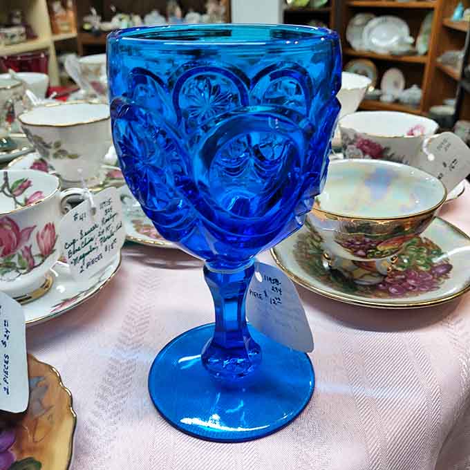 That electric blue Depression glass goblet steals the spotlight among delicate teacups &ndash; a rare find that collectors dream of discovering.