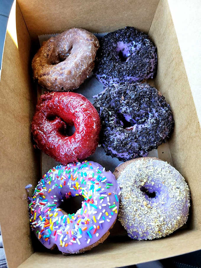 A half-dozen box showcasing the full spectrum from classic chocolate to vibrant purple ube, like a edible rainbow that makes choosing just one flavor impossible.