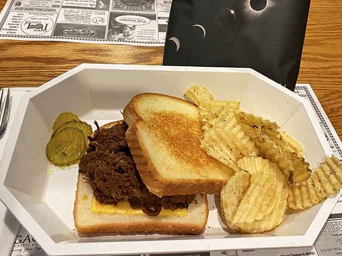 The pulled pork sandwich arrives as a masterpiece of smoky, tender meat piled high between toasted bread with a pickle on the side.