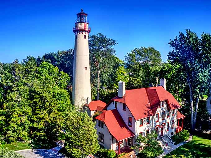 The lighthouse tower reaches skyward through a canopy of trees, its white column playing peekaboo with visitors approaching through the wooded grounds.