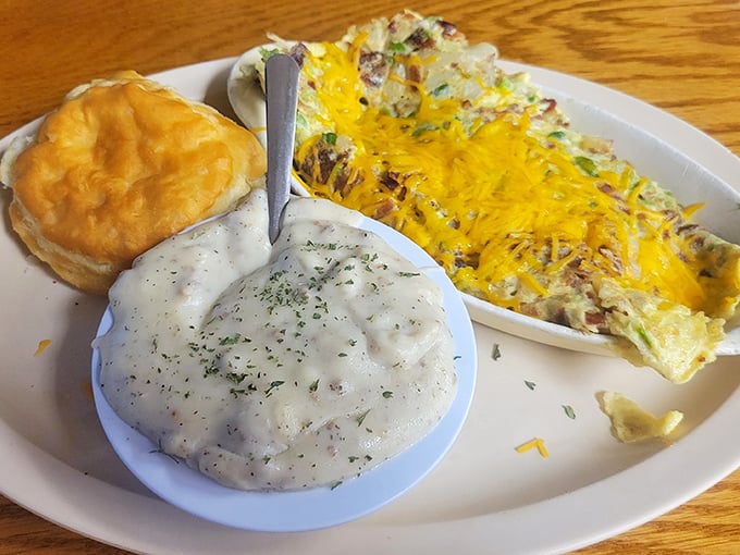 The breakfast trifecta: fluffy biscuits drowning in gravy, a cheese-loaded omelet, and a golden biscuit standing by.