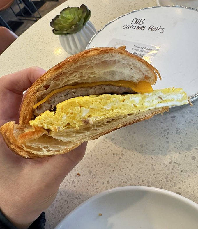 A cross-section reveals the engineering marvel inside &ndash; layers of buttery croissant embracing eggs, cheese, and savory fillings in perfect harmony.