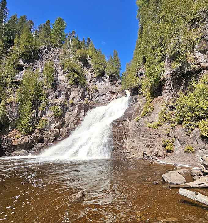 The pool at the base swirls with brown water against dark volcanic rock, wild and untamed.