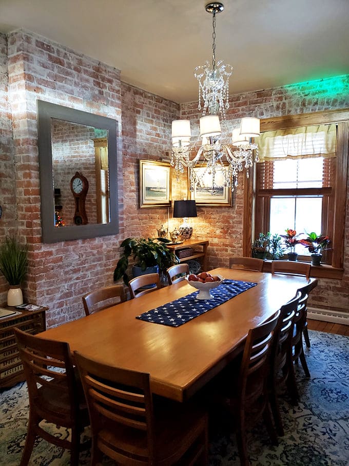 Exposed brick walls and a crystal chandelier create an unexpected elegance in the dining room, where strangers become friends over shared meals.