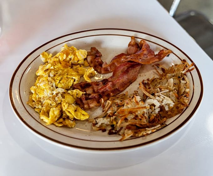 The breakfast trinity: perfectly scrambled eggs, bacon cooked to that magical point between chewy and crisp, and hash browns worth fighting for.